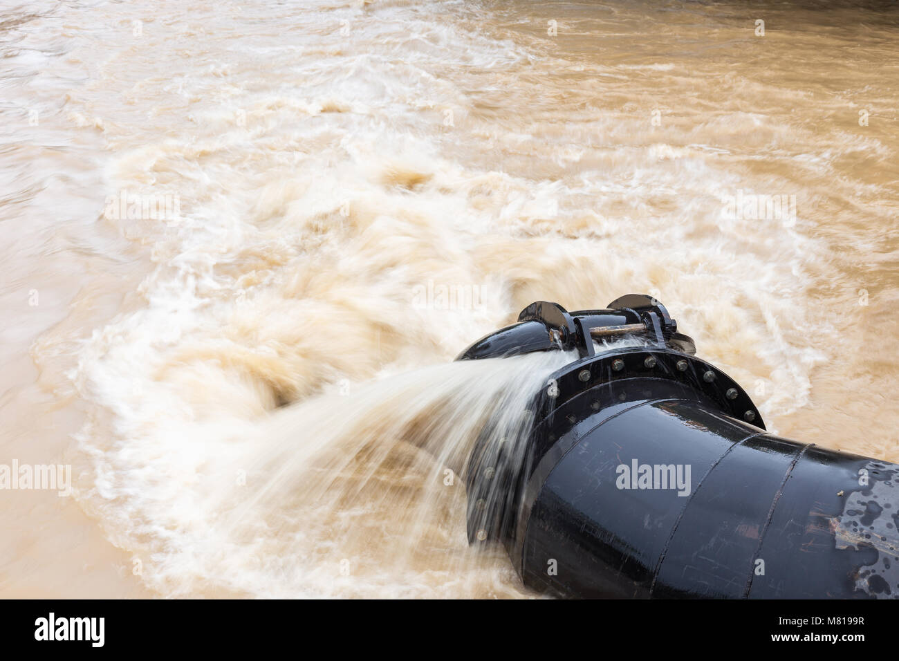 Black large water pipe while pumping flooding water into the river ...