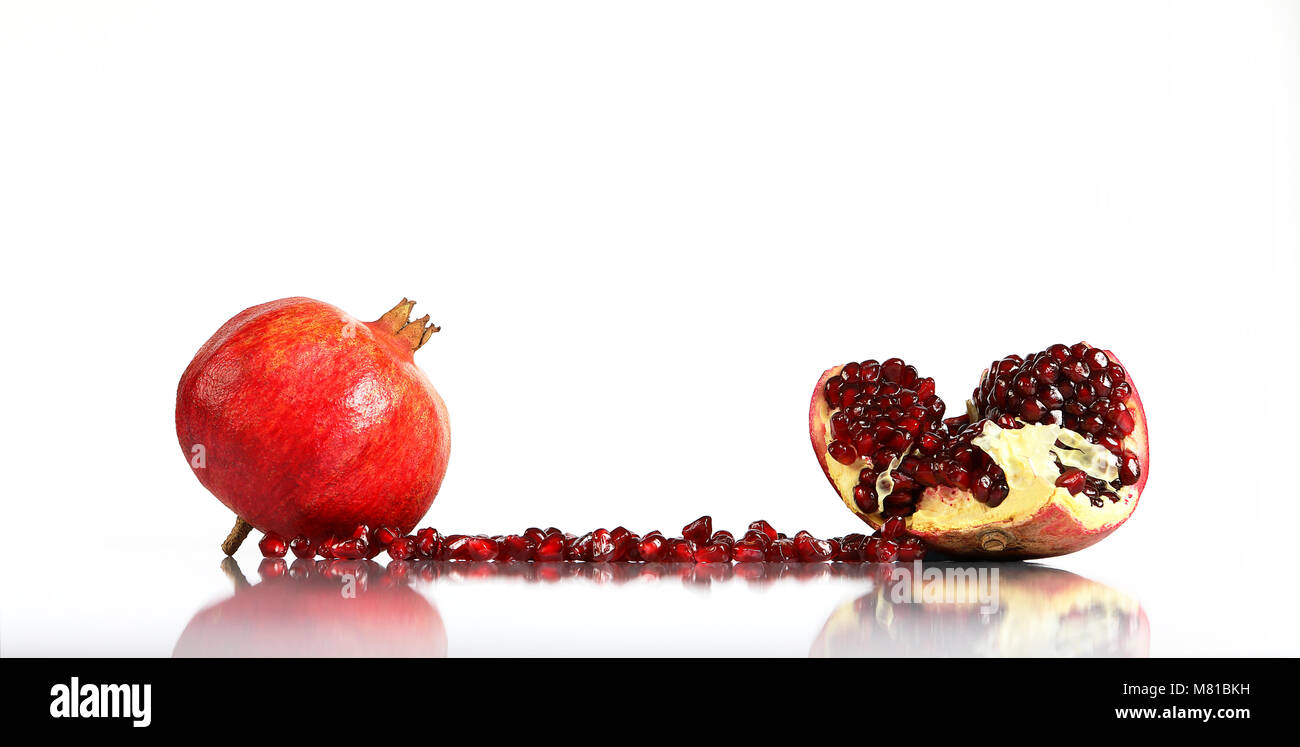 Fresh ripe pomegranate fruits and seeds on white reflective surface and ...