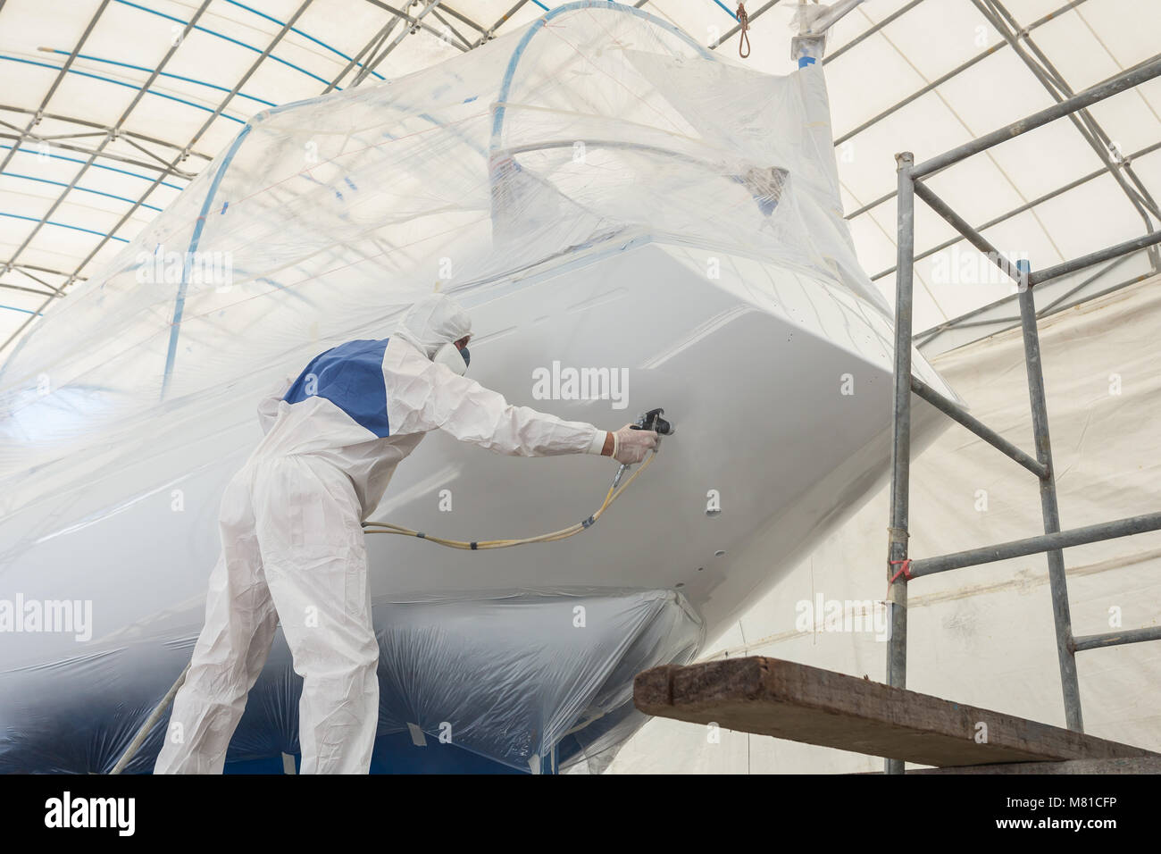 Worker wearing protective uniform and spraying paint to the boat ...