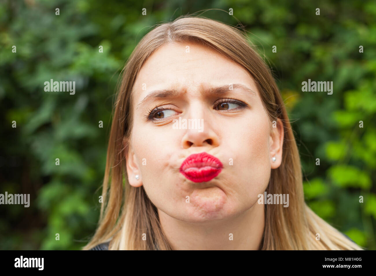 Young woman making a grimace outdoor, green background. Sad - grumpy ...
