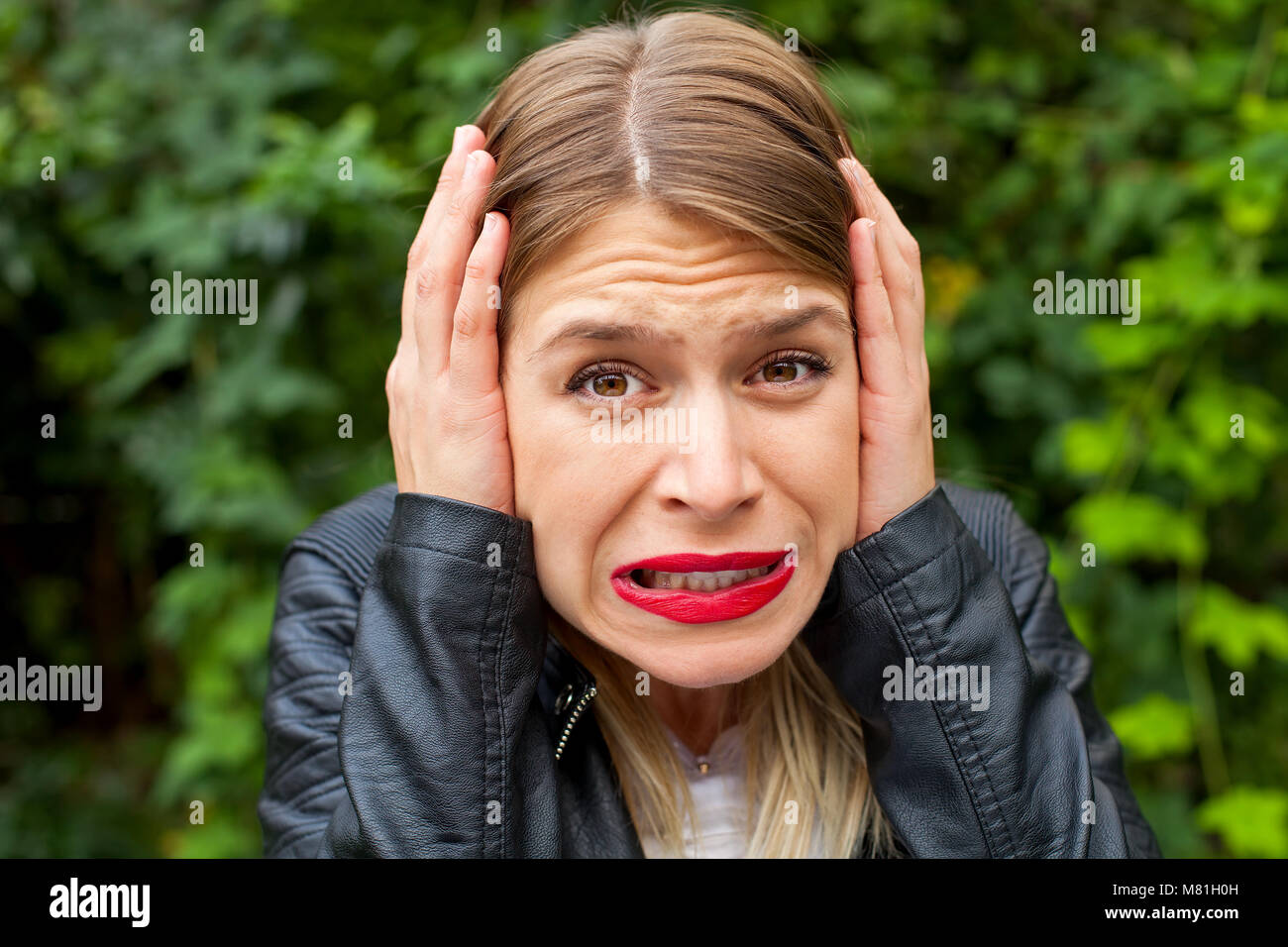 Young woman making a grimace outdoor, green background. Sad - grumpy ...
