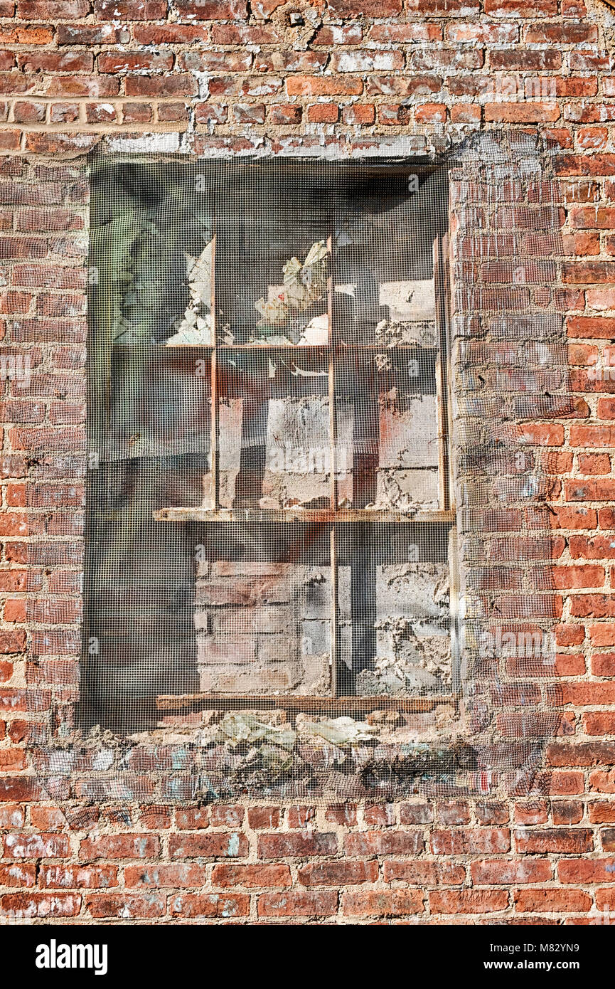 A wire screen covers up a bricked-up window on the outside of a red ...