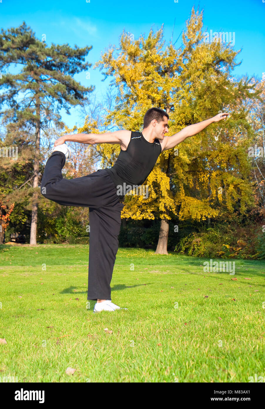 Attractive young man doing exercise in autumn park Stock Photo - Alamy