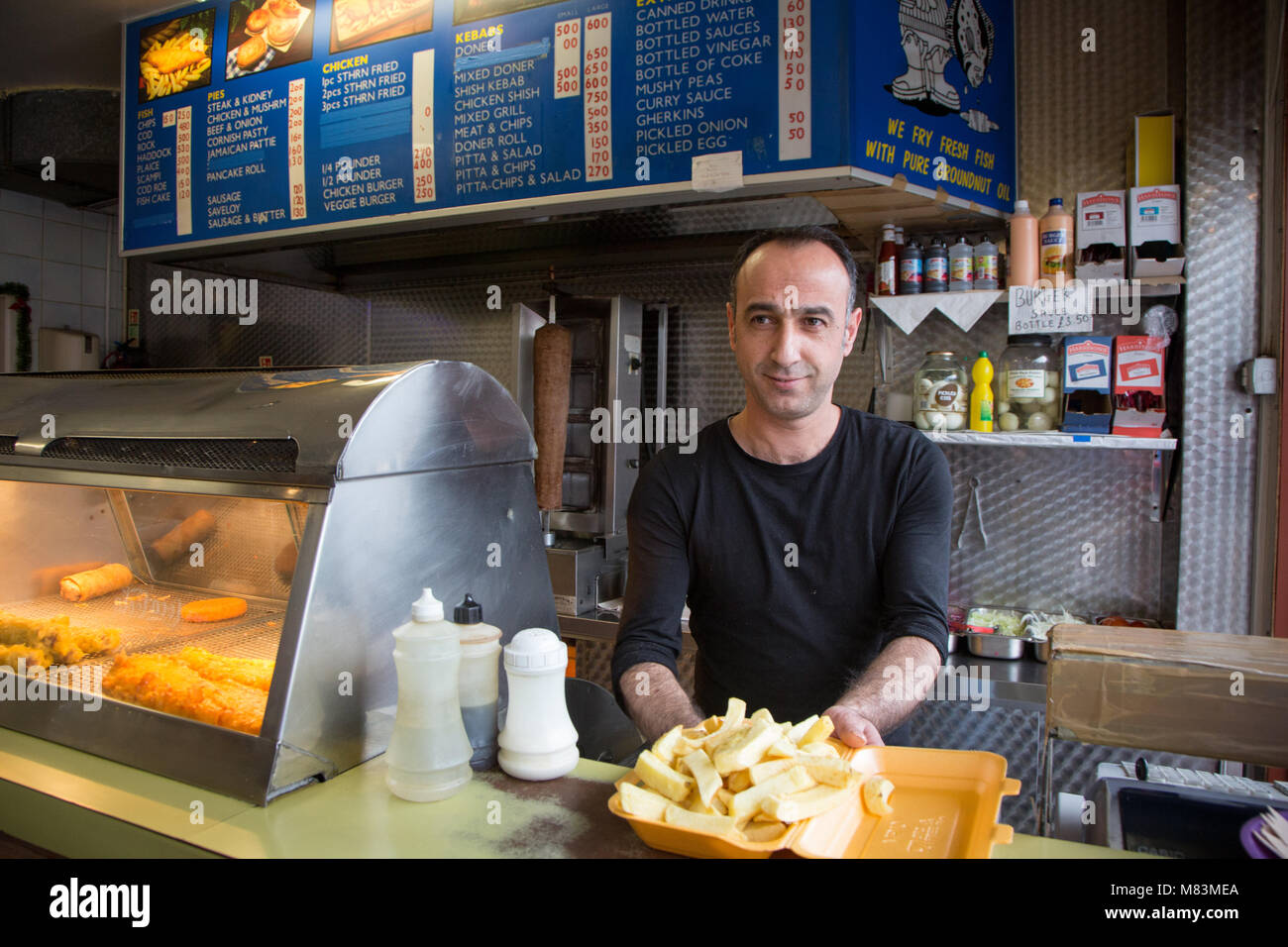 Turkish man serving chips at a takeaway fish and chips restaurant Stock ...