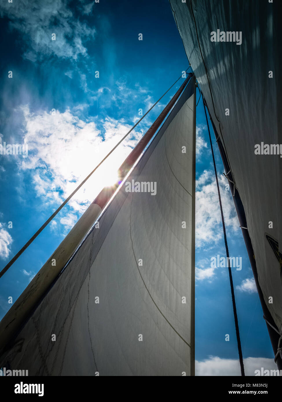 White sail against blue sky, clouds and sun ray Stock Photo - Alamy