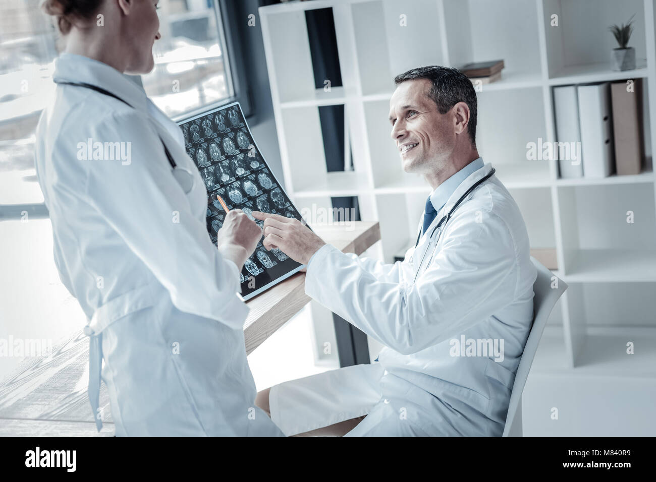 Pleasant skilled doctor sitting and looking at his colleague Stock ...