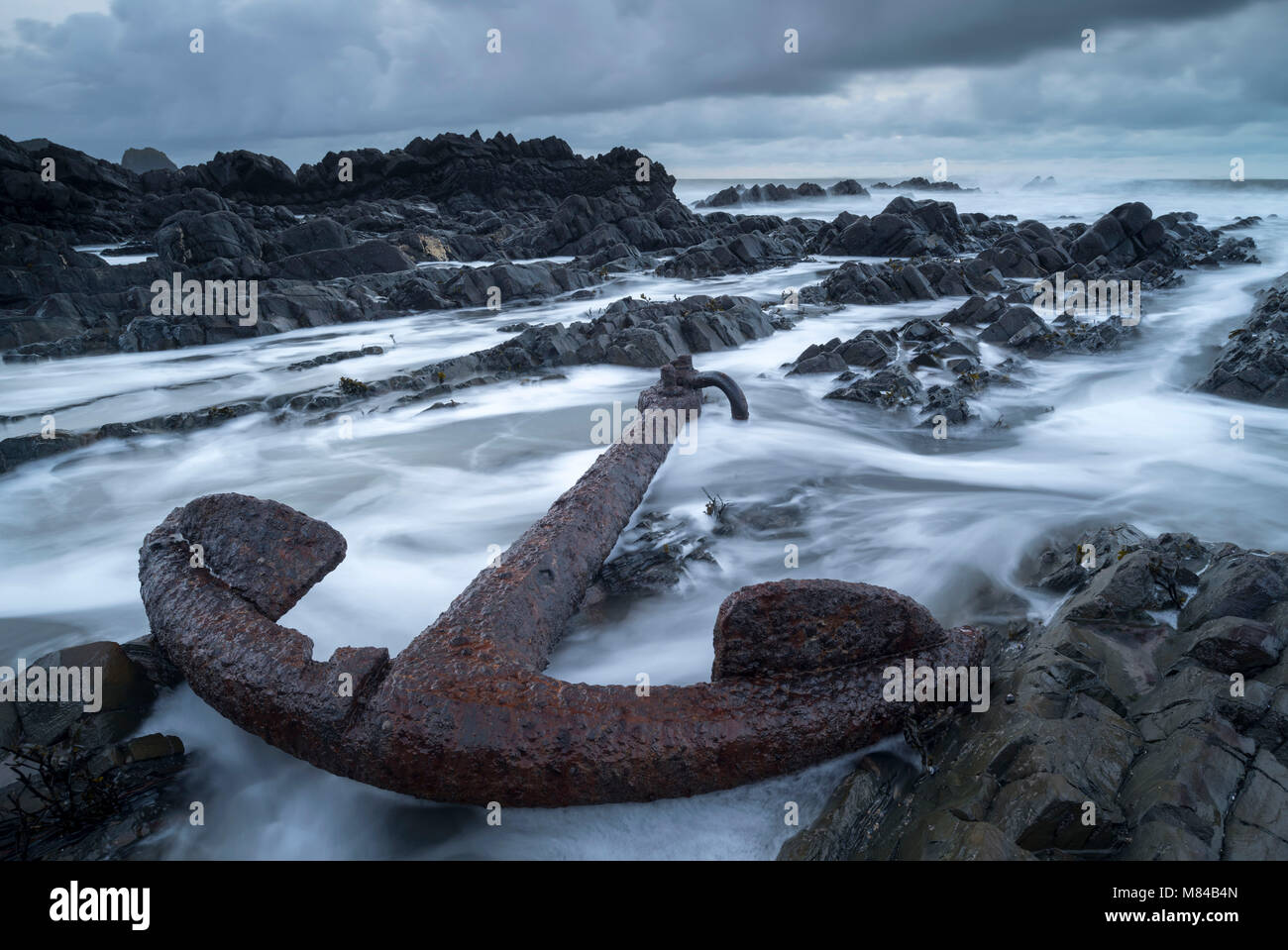 Large rusted anchor from a shipwreck on rocky seashore, Devon, England ...
