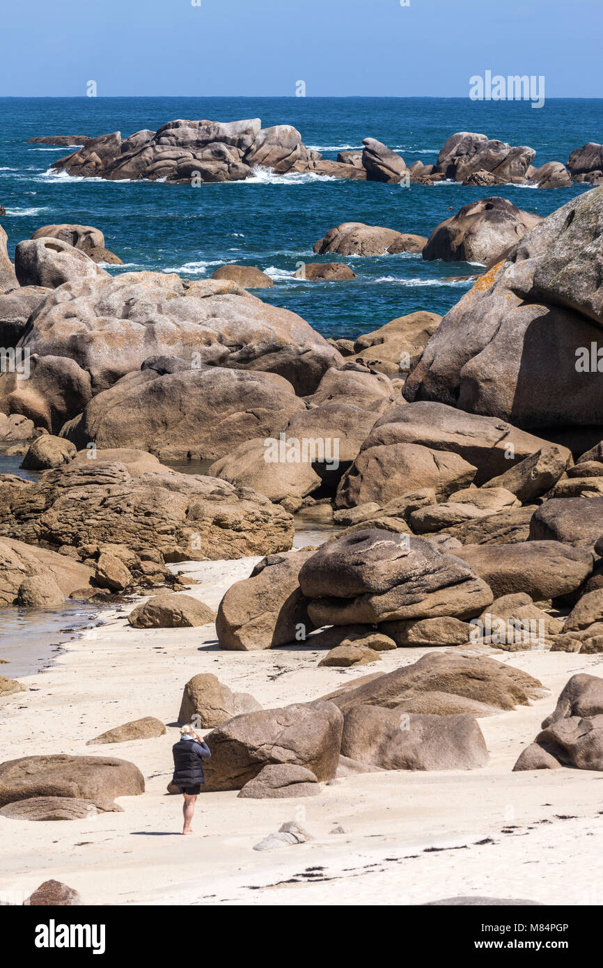 Woman stands on the sandy beach with big rocky shore in front of her ...