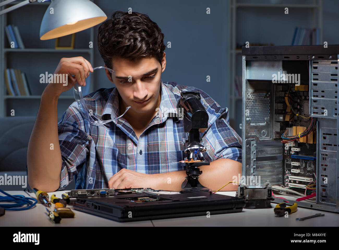 Repairman trying to repair laptop with miscroscope Stock Photo - Alamy
