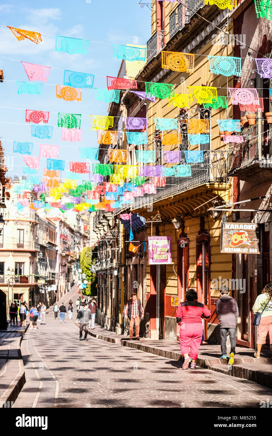 Mexicans walking on cobblestone street with sun lit colorful banner ...