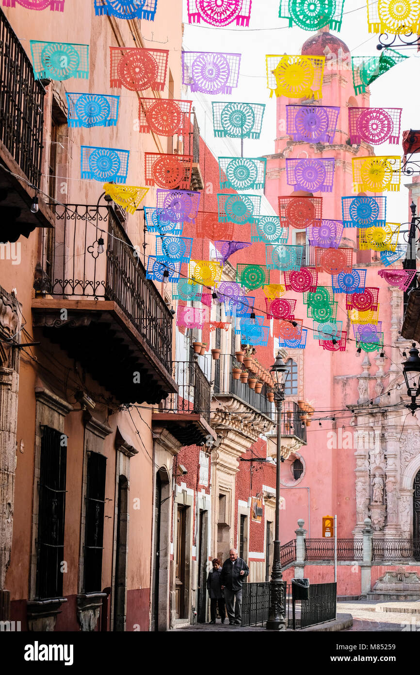 Mexicans walking on cobblestone street with sun lit colorful banner ...