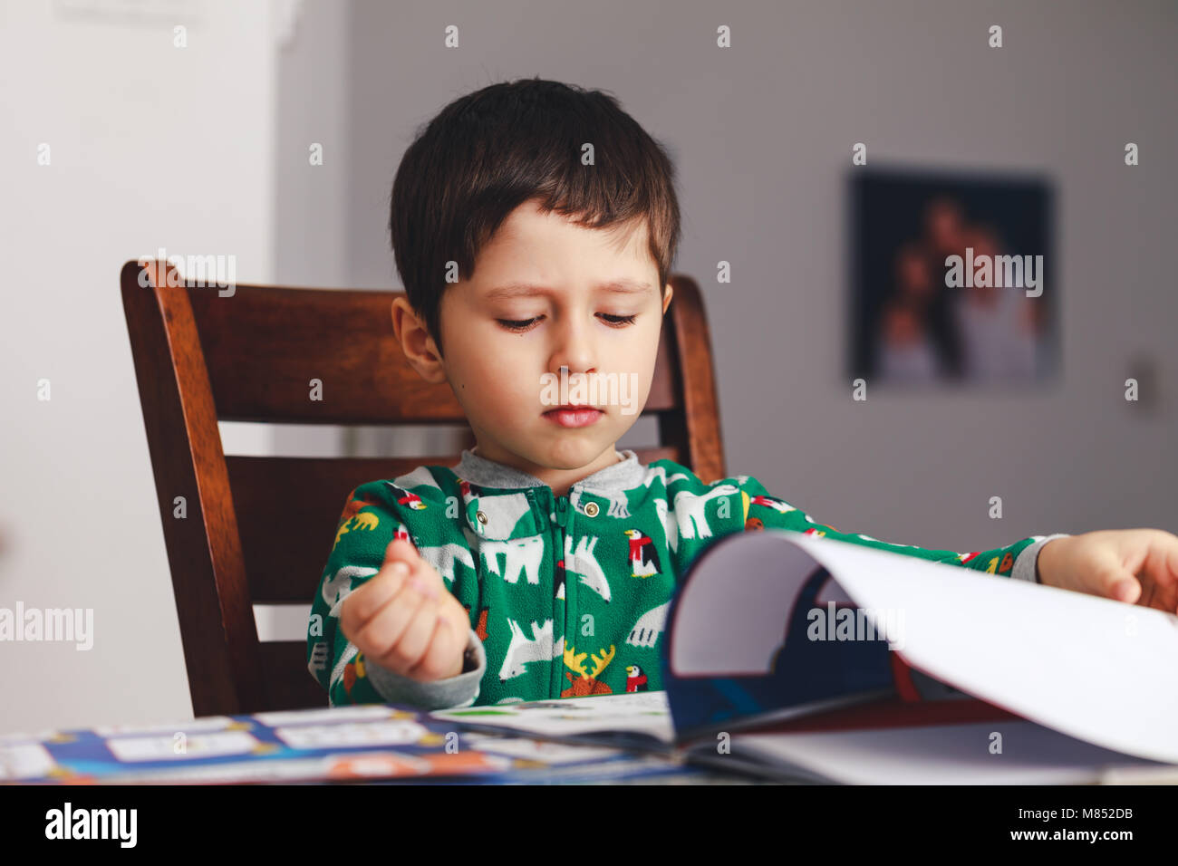 Cute boy reading a book while sitting at table, indoor shoot. Little ...