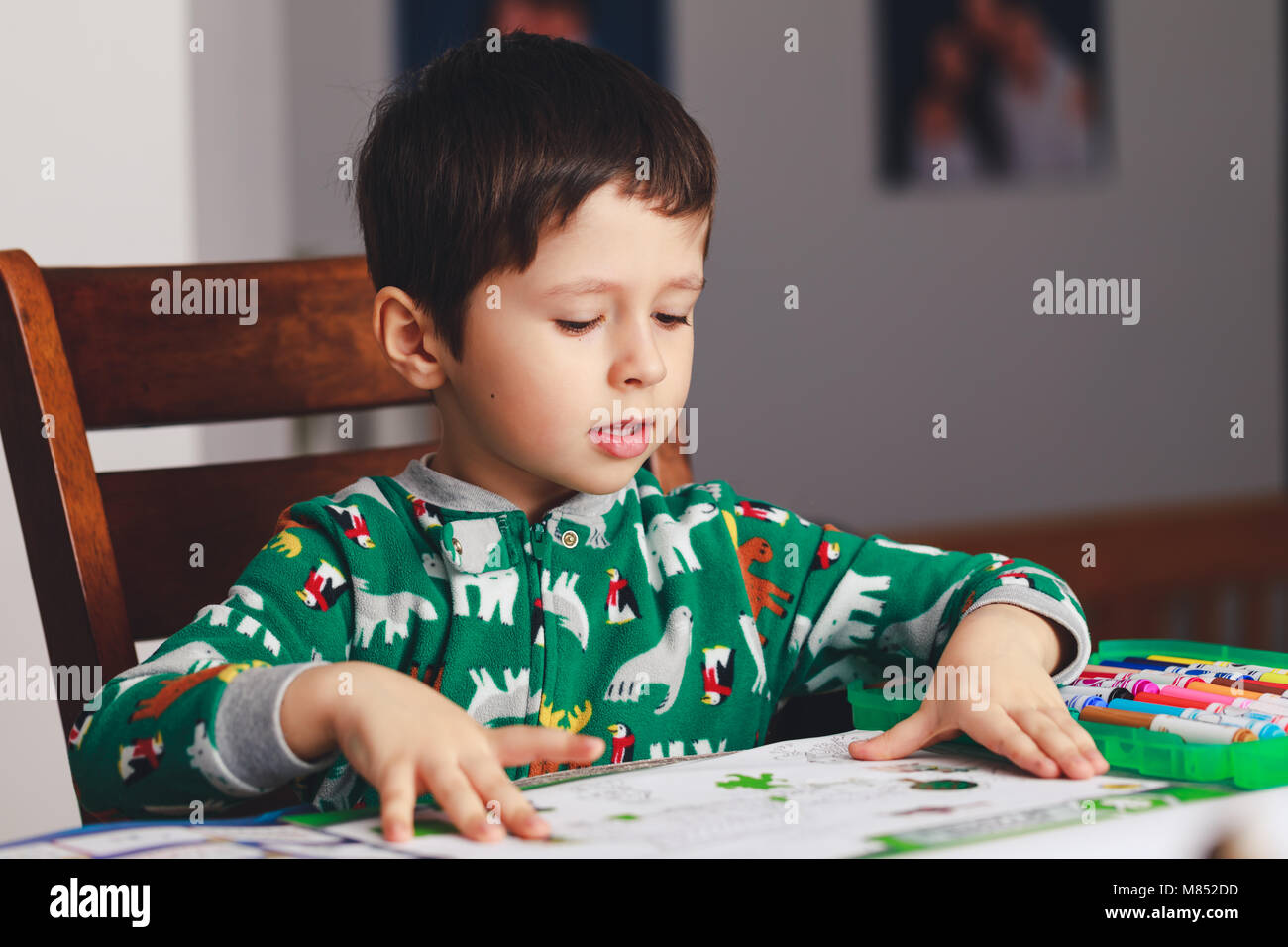Preschool kid reading a book while sitting at table, indoor shoot ...