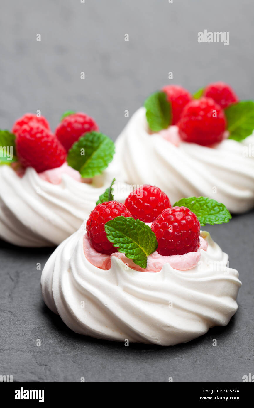 Mini Pavlova meringue nests with raspberries and mint on black stone ...