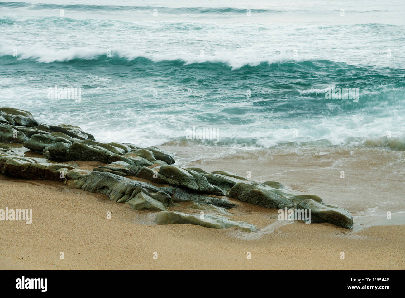 Smooth wet rocks are revealed as water draws back against a wave about ...