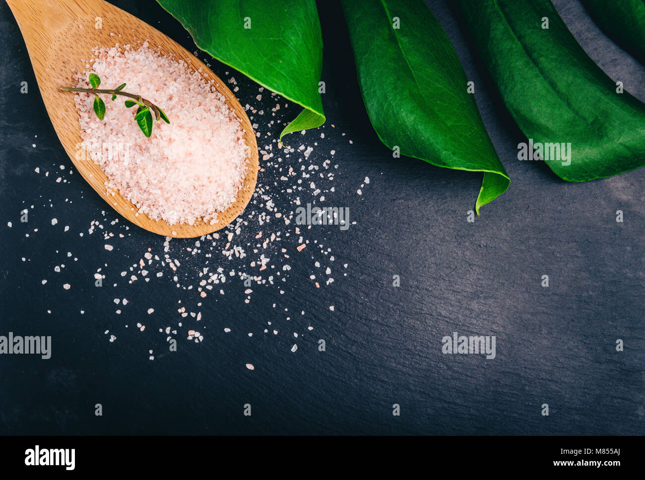 Himalayan salt in bamboo spoon on black slate plate with monstera leaf ...