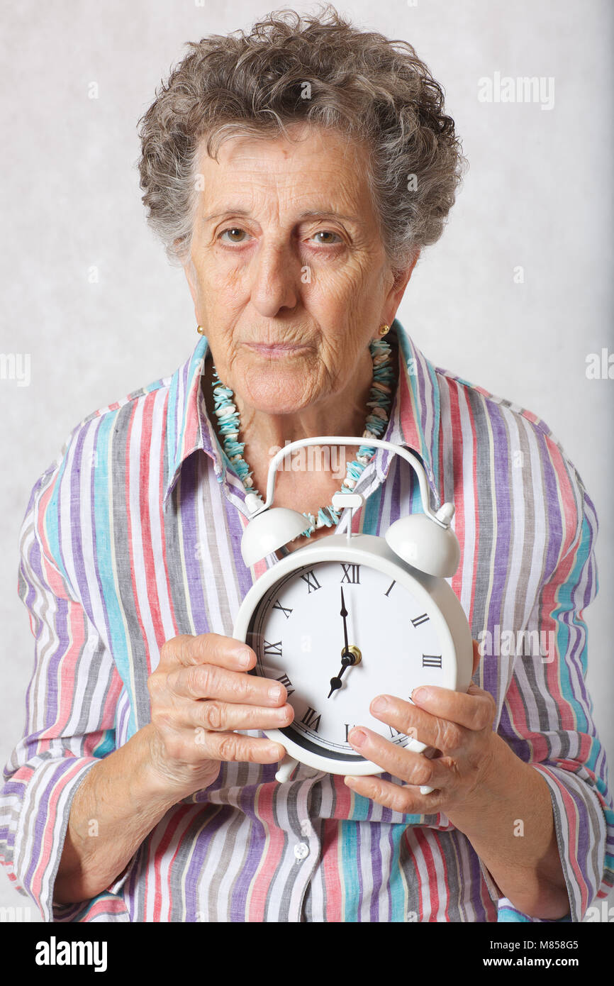 Senior woman between 70 and 80 years old shows vintage alarm clock ...
