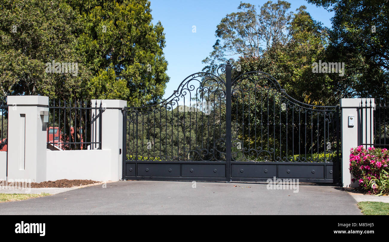 Metal driveway entrance gates set in brick fence with garden trees in ...