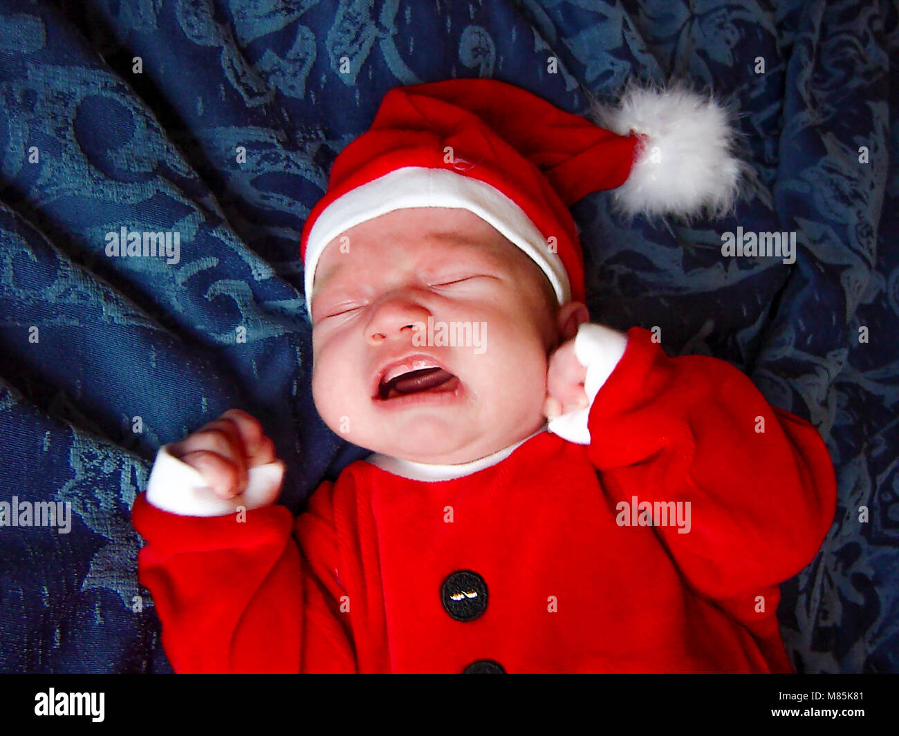 Unhappy Santa little baby crying on blue background Stock Photo - Alamy