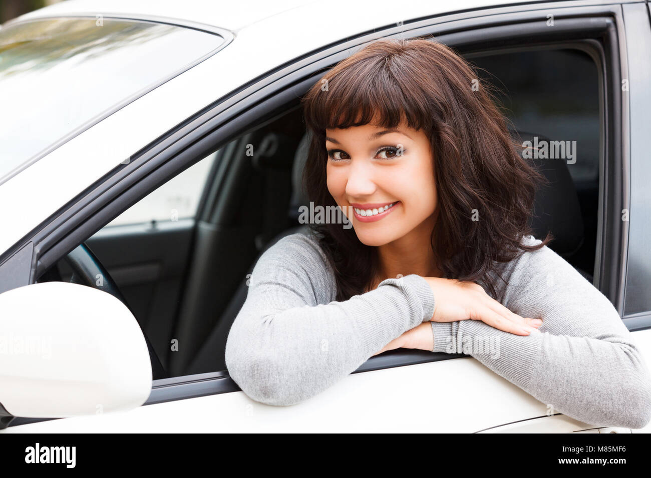 Happy owner of a new car. Young pretty woman driver smiling to you ...