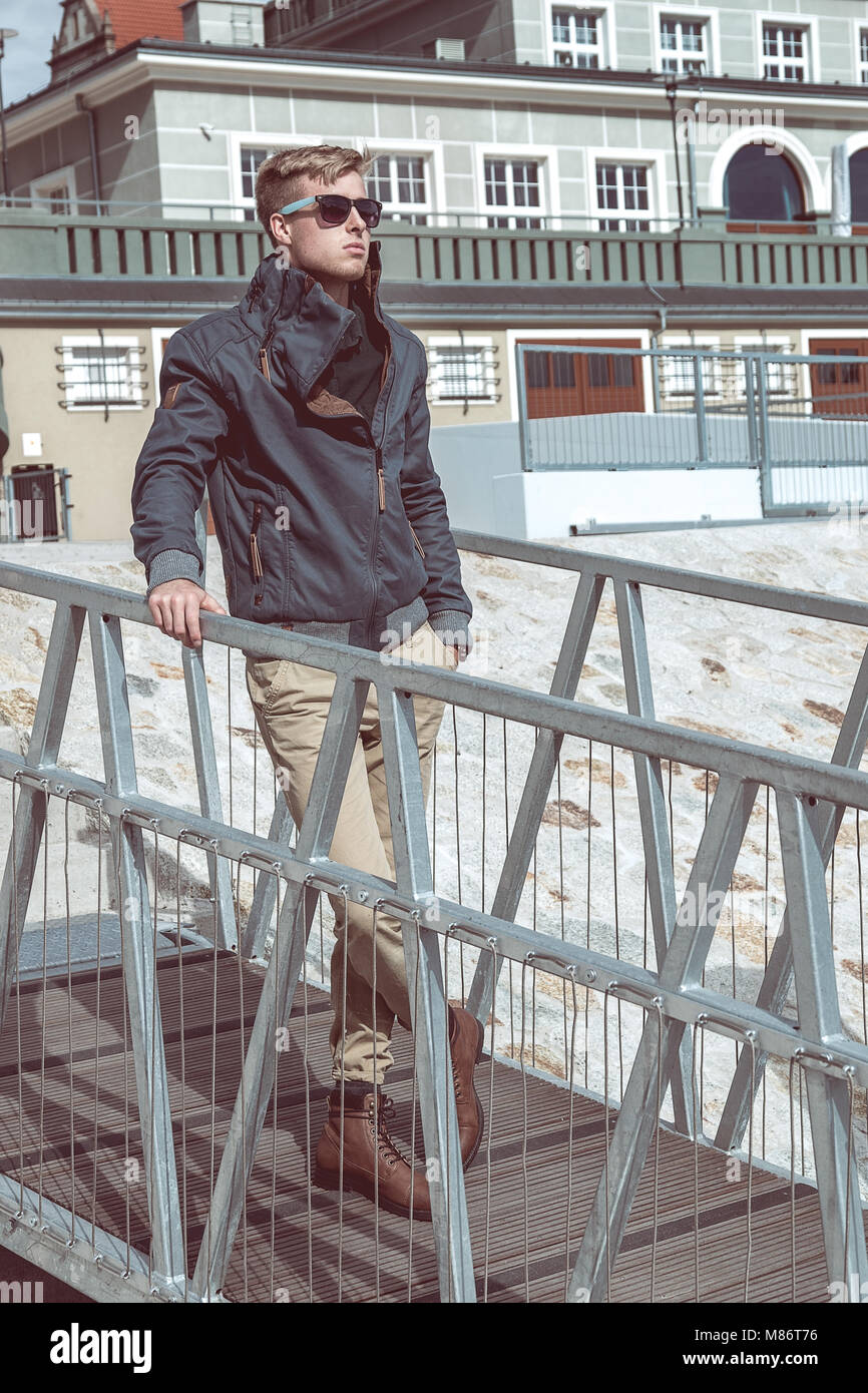 Handsome young man keeping arms crossed on the balustrade and looking ...
