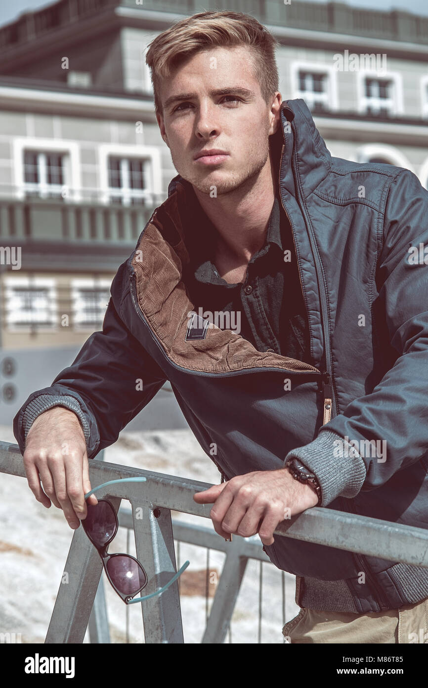 Handsome young man keeping arms crossed on the balustrade and looking ...