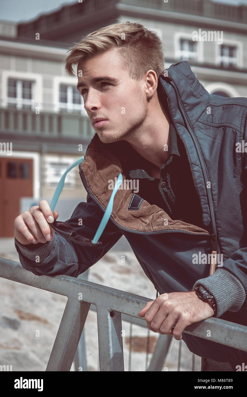Handsome young man keeping arms crossed on the balustrade and looking ...