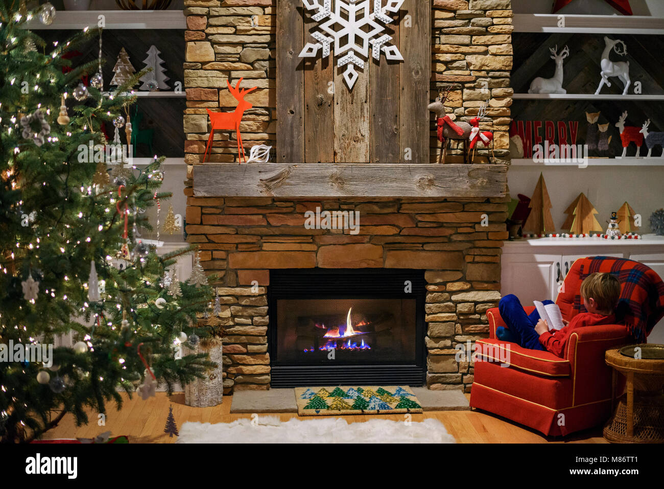 Boy sitting by the fireplace reading a book at Christmas Stock Photo ...
