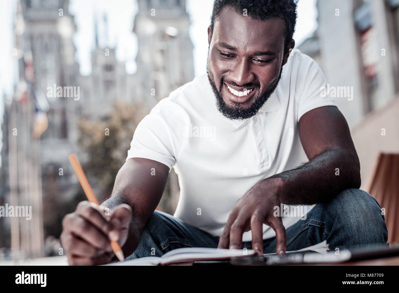 Cheerful millennial guy smiling while writing something down Stock ...