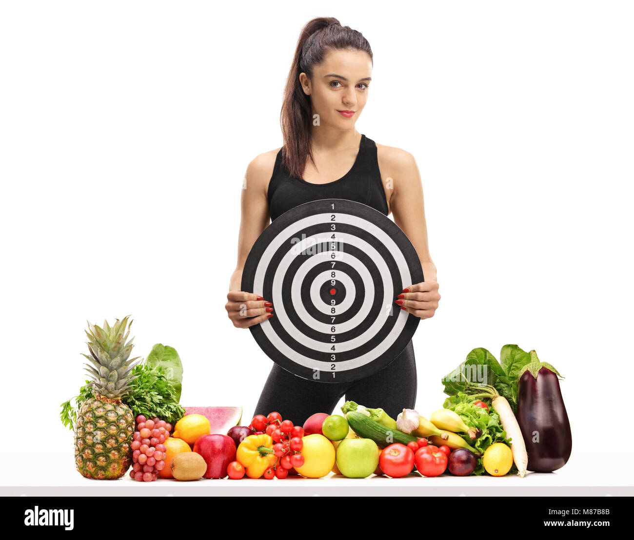 Fitness girl holding a target behind a table with fruit and vegetables ...