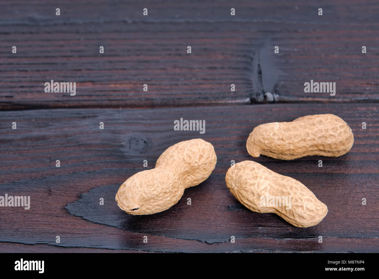 Three peanuts on a wooden table Stock Photo - Alamy