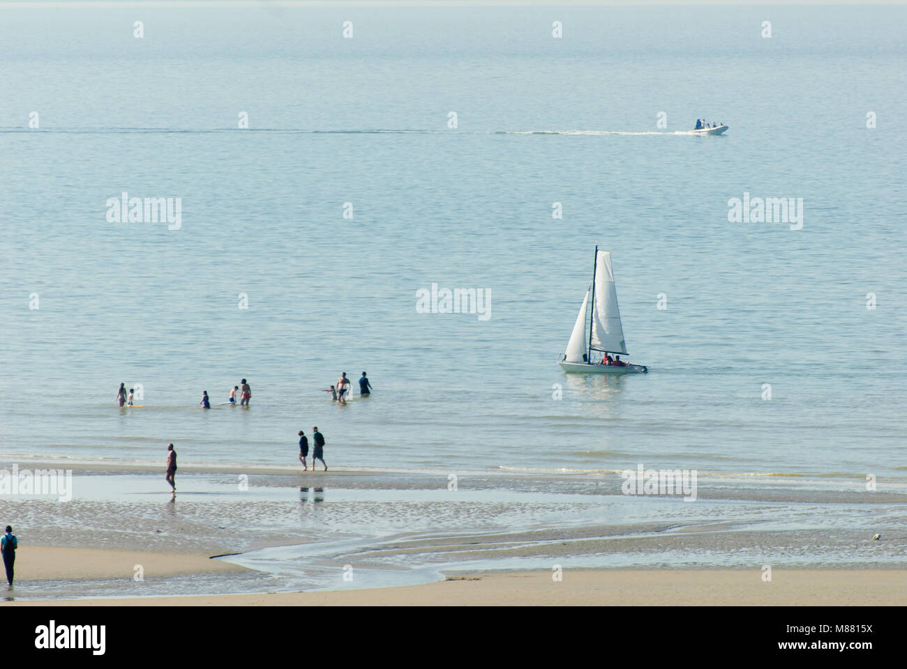people on the beach watching a sailing boat a coasting near the sand at ...