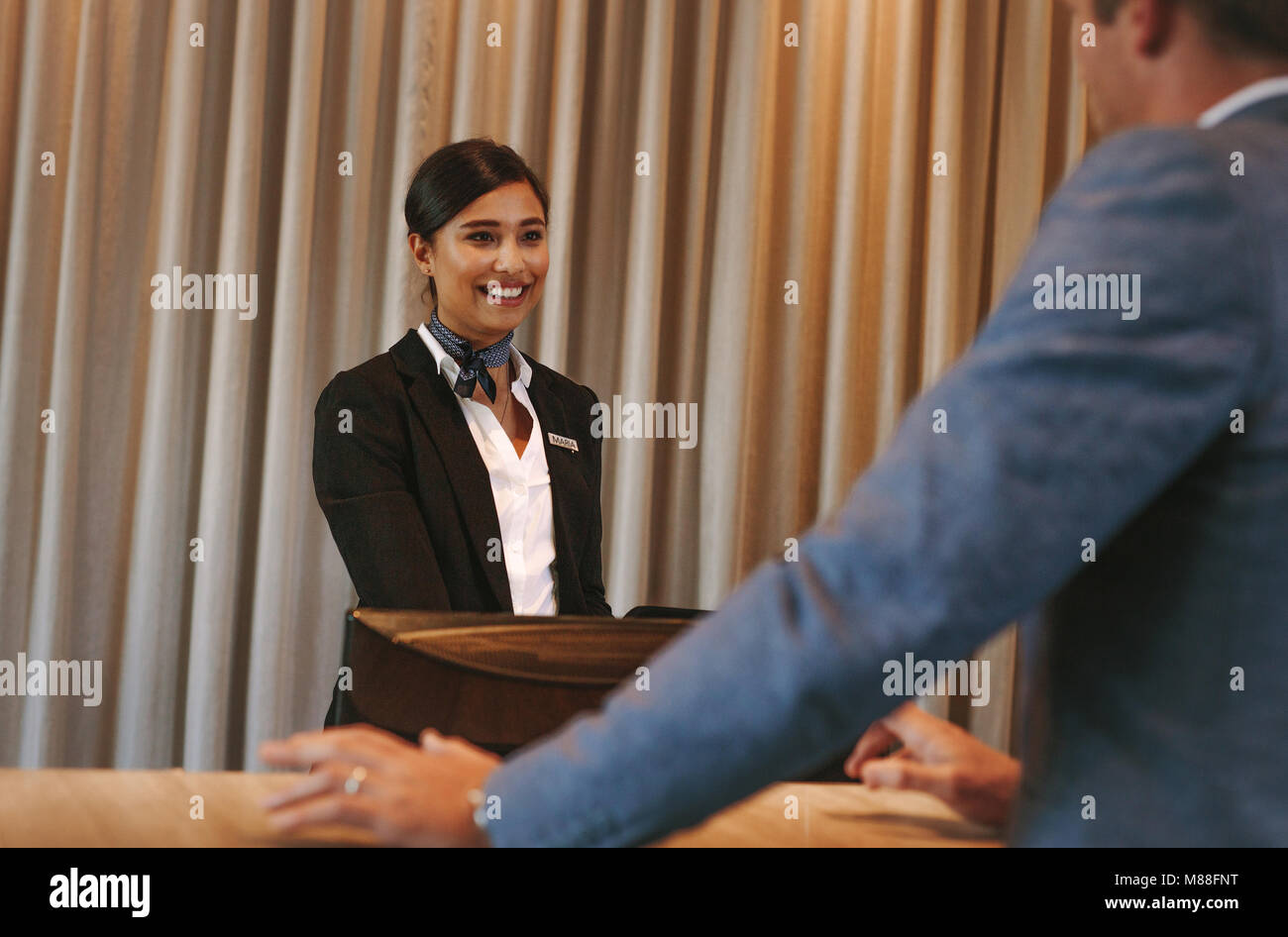 Female hotel receptionist attending a guest at reception counter. Happy ...