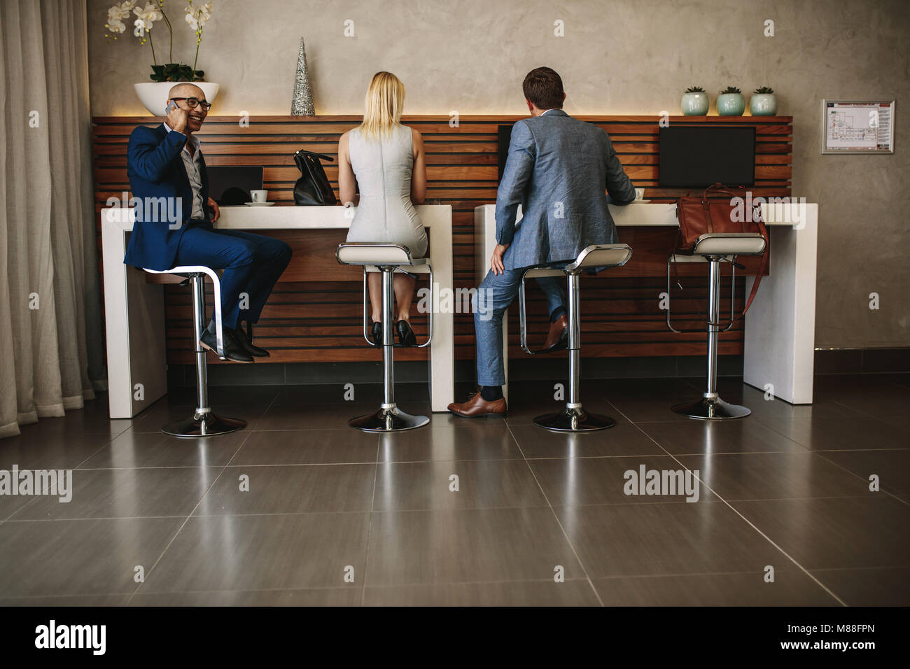 Rear view shot of travelers sitting at free internet service counter in ...