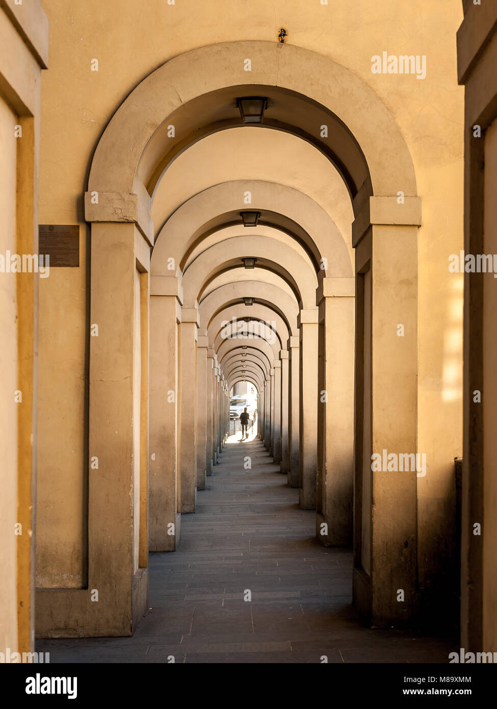 Passageway in Florence (Italy) with round arches and person at the end ...