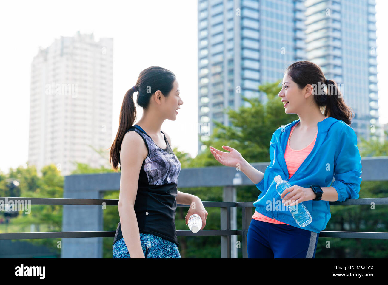 Two healthy female runners taking a break chatting with city background ...