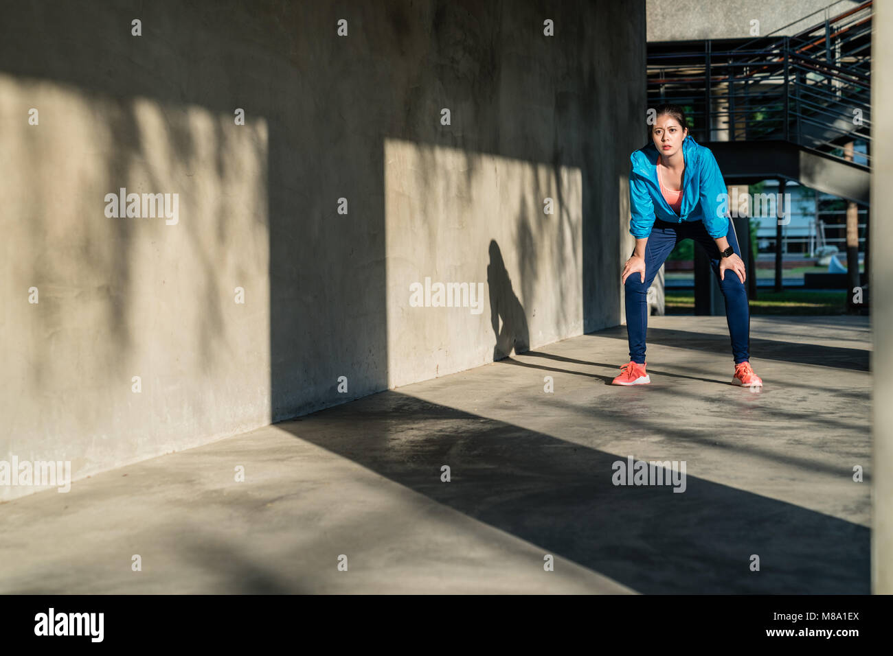 Female runner taking a break standing bent over and catching her breath ...