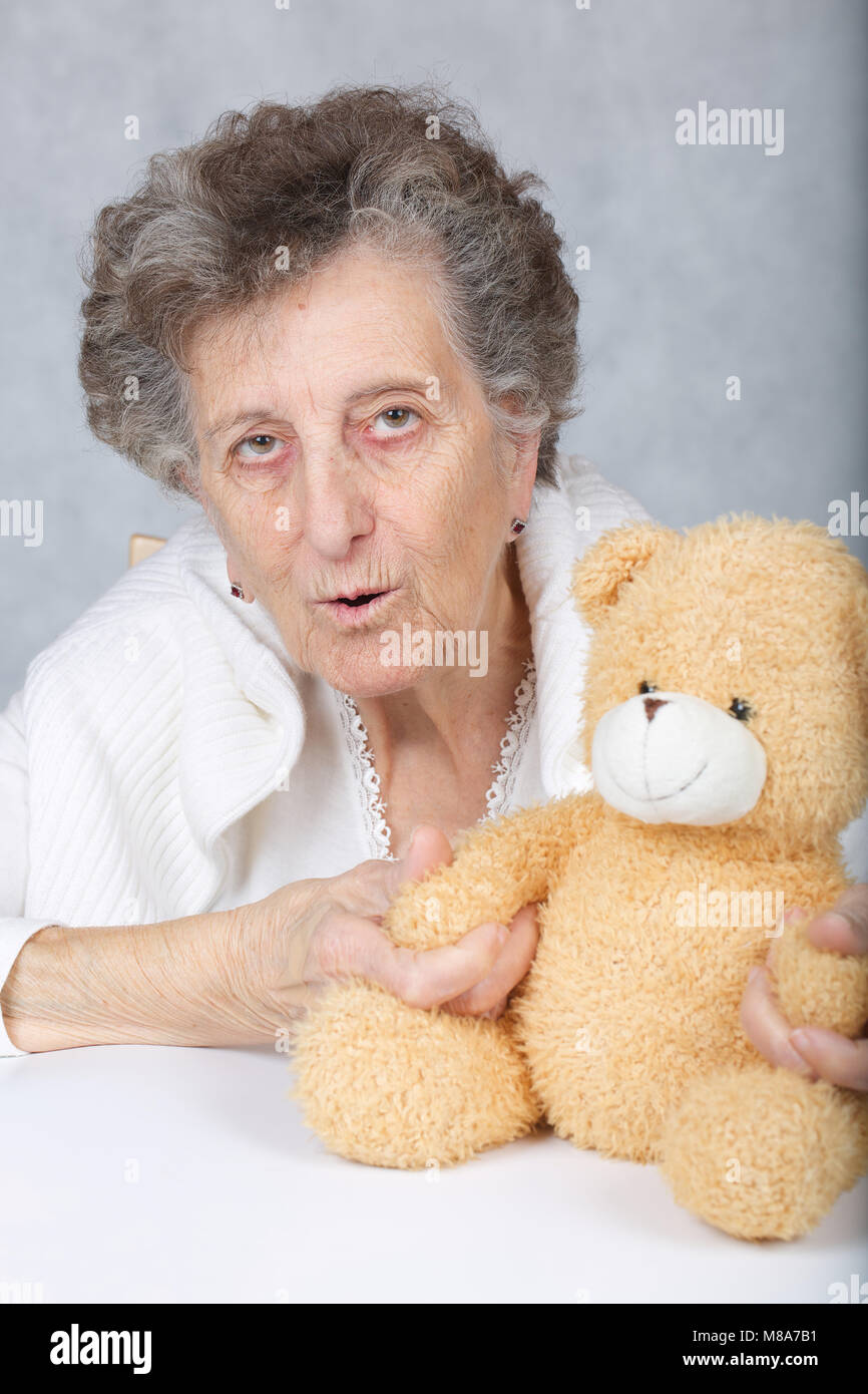 Senior woman between 70 and 80 years old sits with plush teddy bear at ...