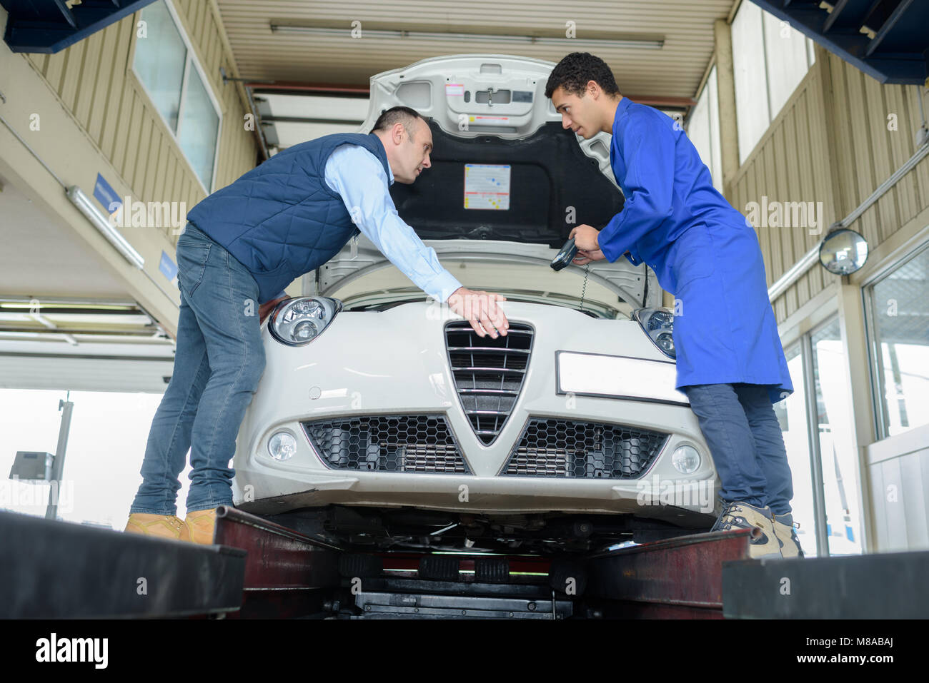 two mechanics working on a car engine at the garage Stock Photo - Alamy