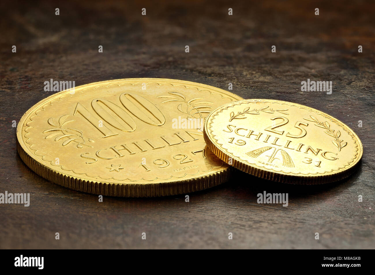 Austrian 25 and 100 Schilling gold coins on rustic wooden background ...