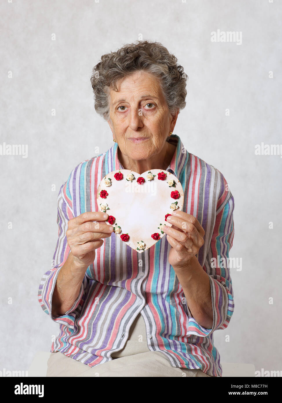 Senior woman between 70 and 80 years old keeps heart in the hands. Gray ...