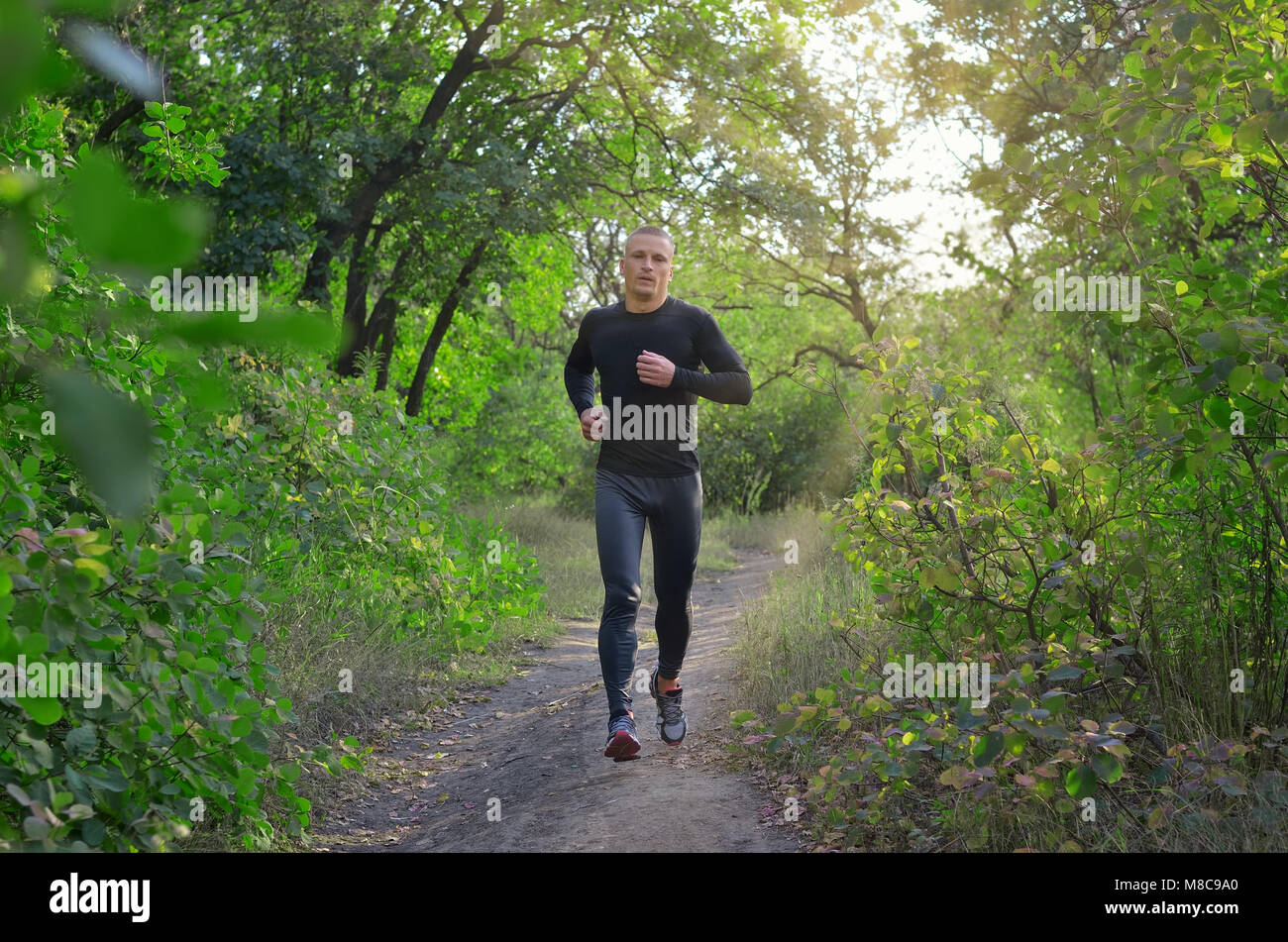 A young strong jogger in a black sports leggins, shirt and sneakers ...