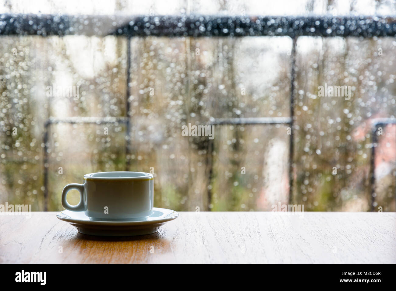 A white espresso cup on a wooden table in front of a glass window ...