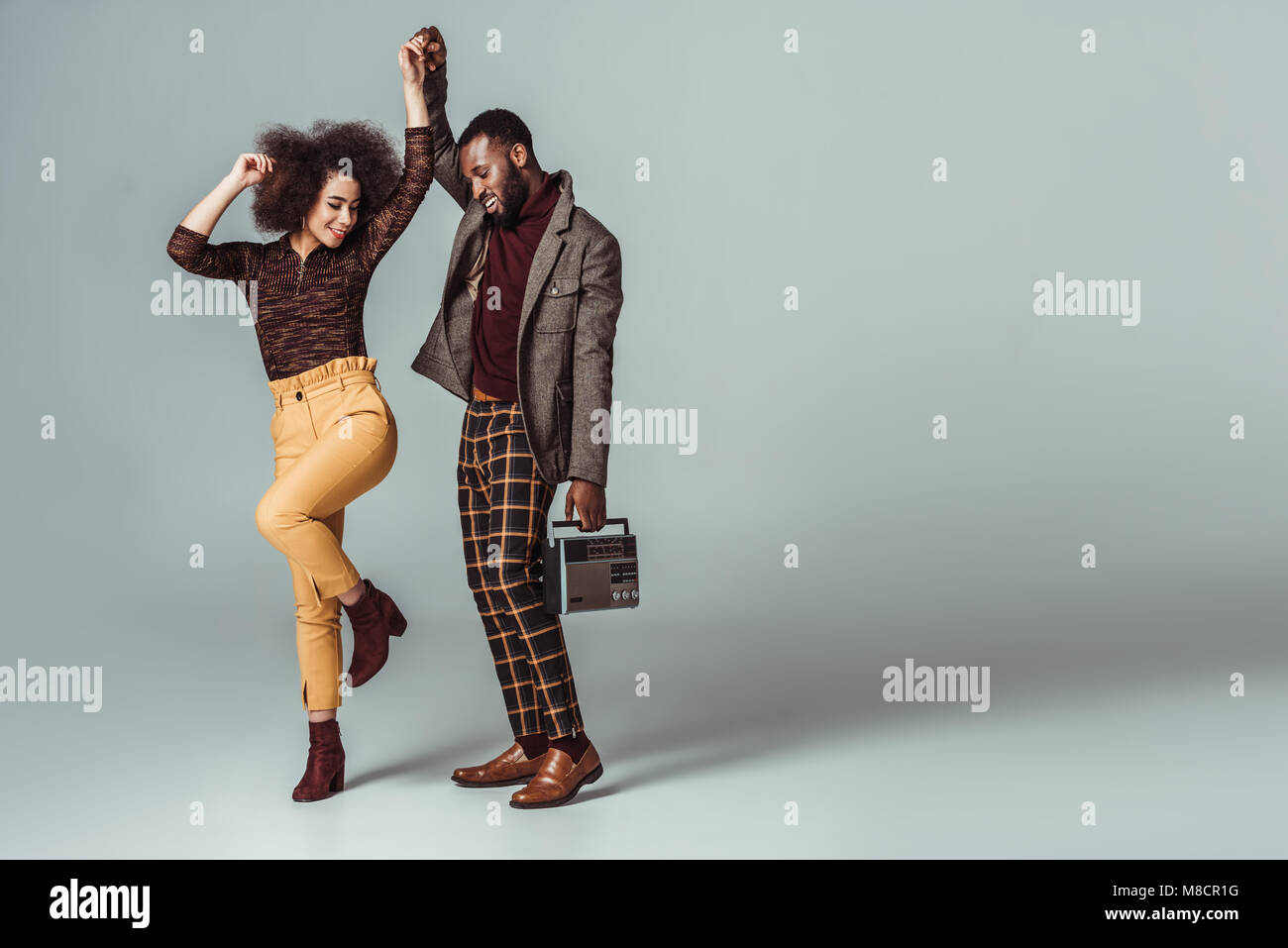 african american retro styled couple dancing with vintage radio on grey ...