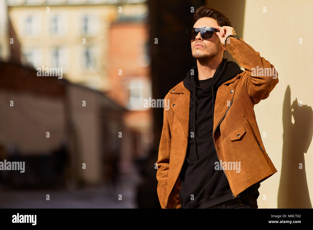 Model looking man stand near the wall and hold his glasses towards the ...