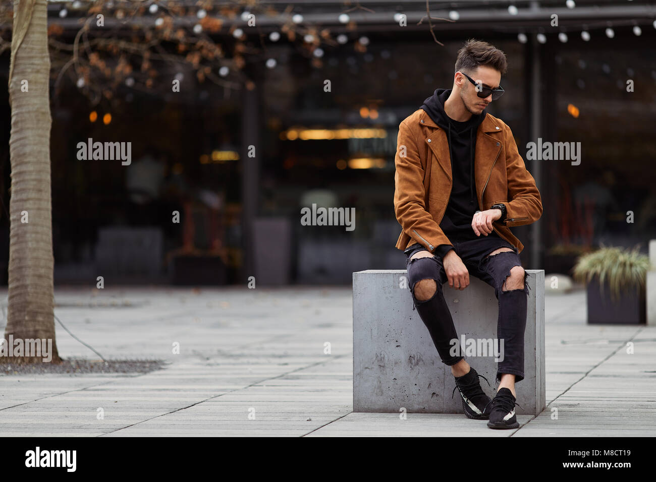 Model looking man sit on the bench in modern park background, look on ...