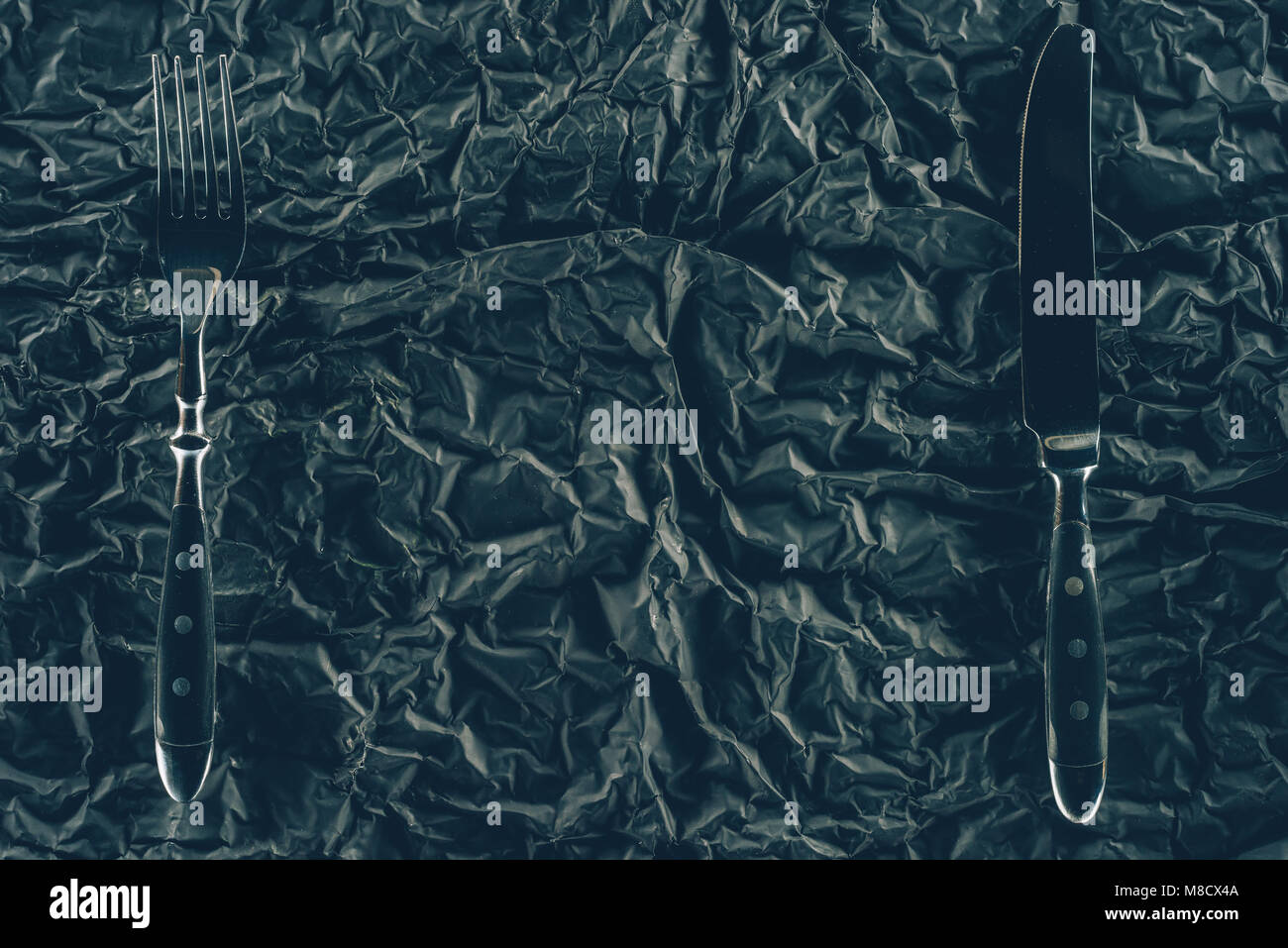 top view of steel fork and knife on dark textured surface Stock Photo ...