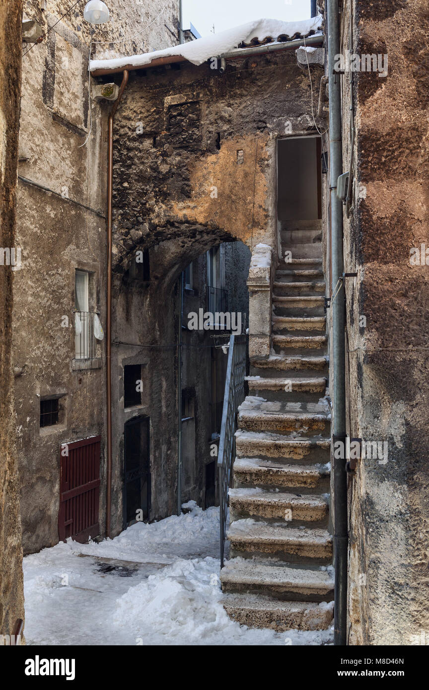 Snow-covered medieval alley with stairway leading to the house and arch ...