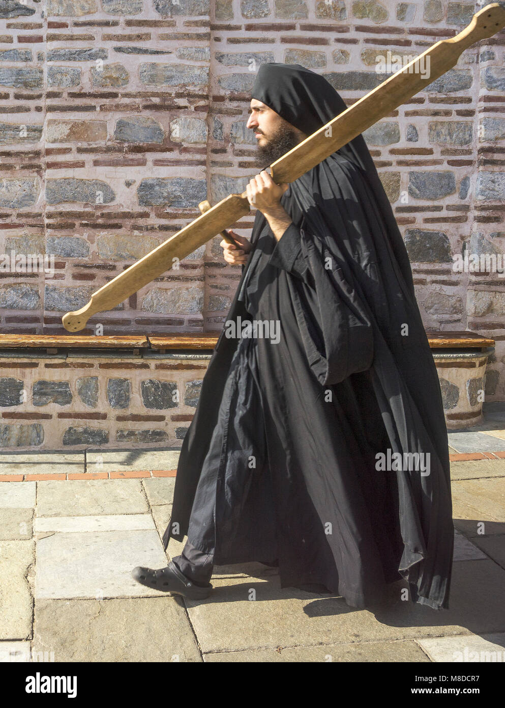 An orthodox monk sounds the call to evening prayer by striking a wooden ...
