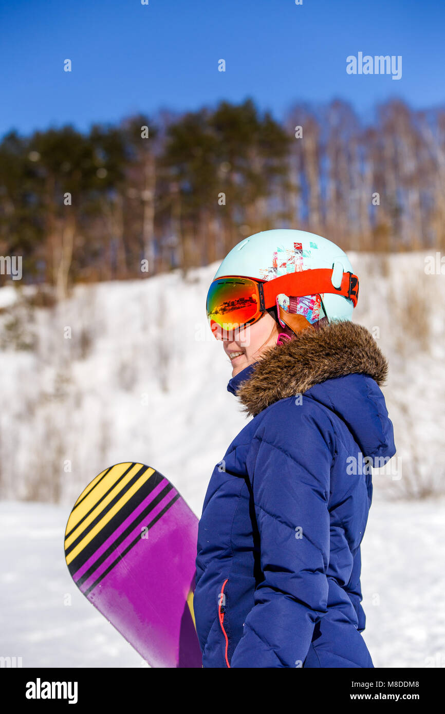 Side view of sporty woman wearing helmet with snowboard looking at ...
